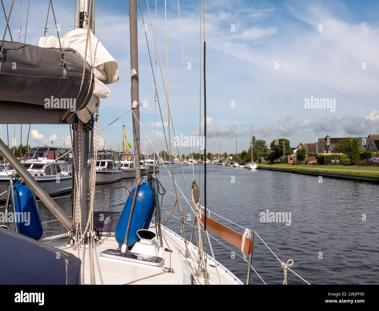 Sailboat with sails down motoring in Zijlroede canal in town of Lemmer, Friesland, Netherlands ...