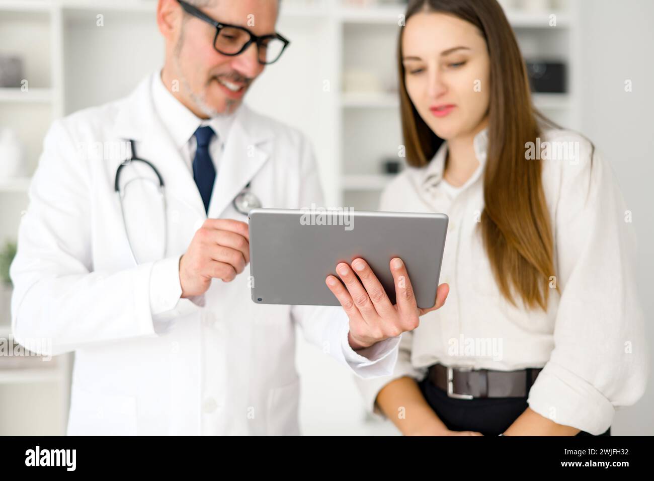 A mature doctor is engaging with a young female patient, showing her ...