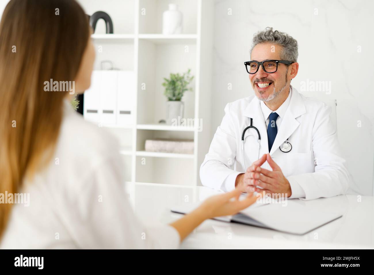 A senior male doctor with grey hair and glasses is seen smiling ...