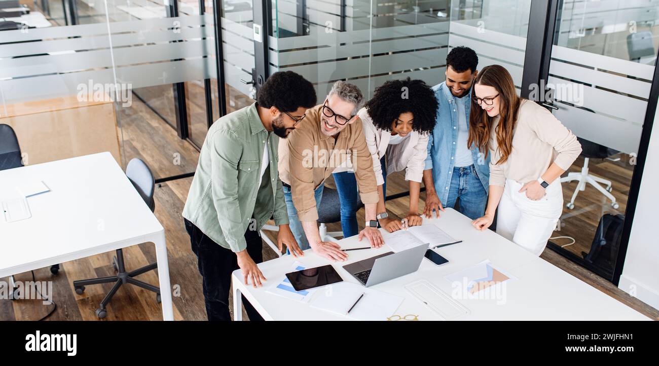 A diverse team is huddled around a table in the office, reviewing ...