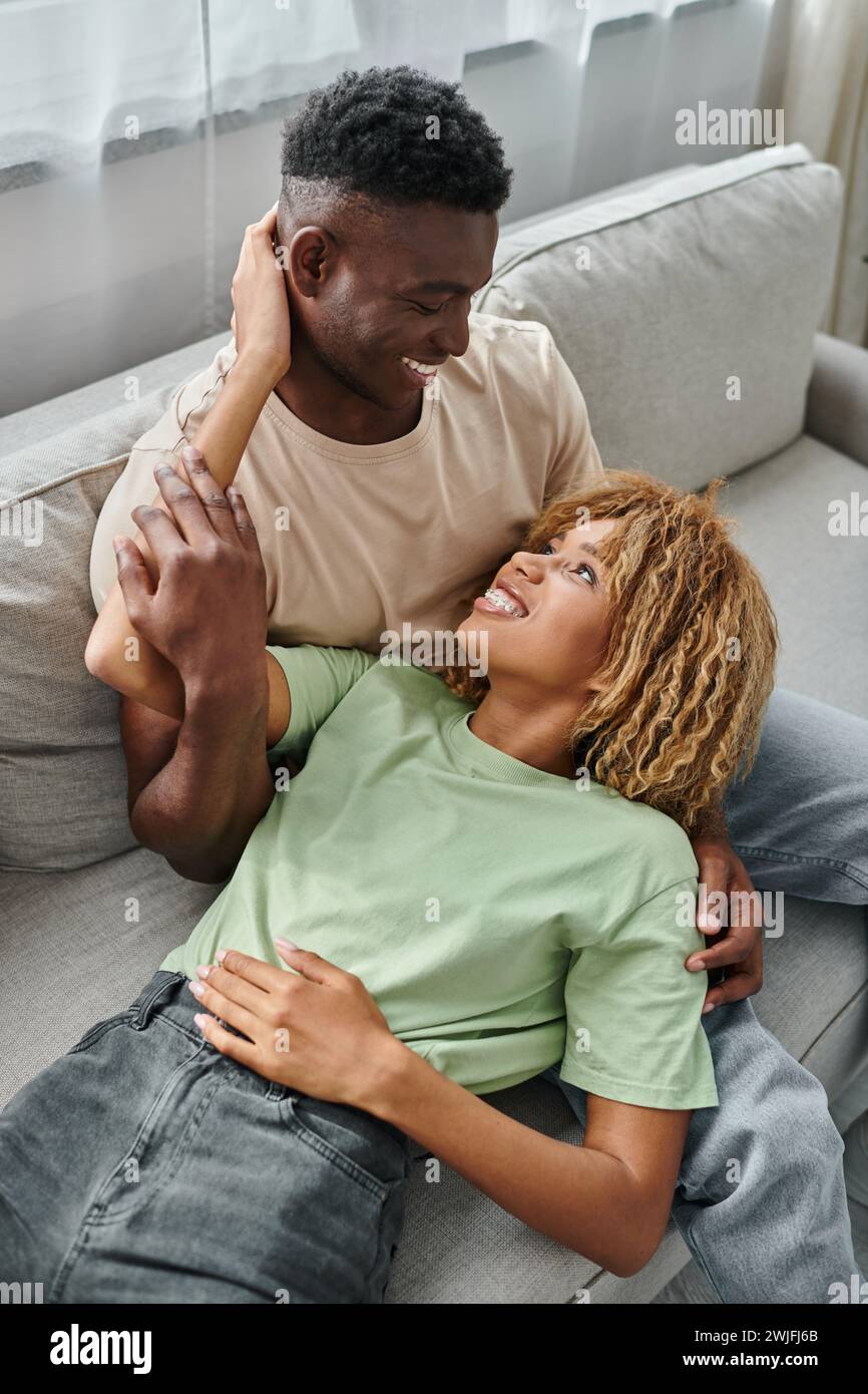 happy african american couple laughing while relaxing on sofa, black ...