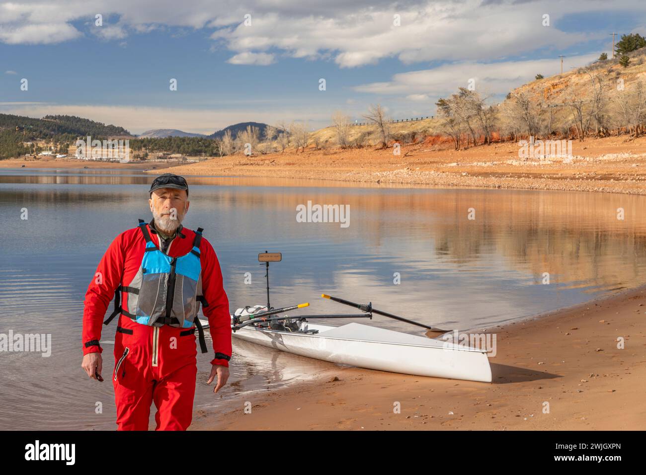 senior man wearing drysuit and life jacket with a rowing shell on lake ...