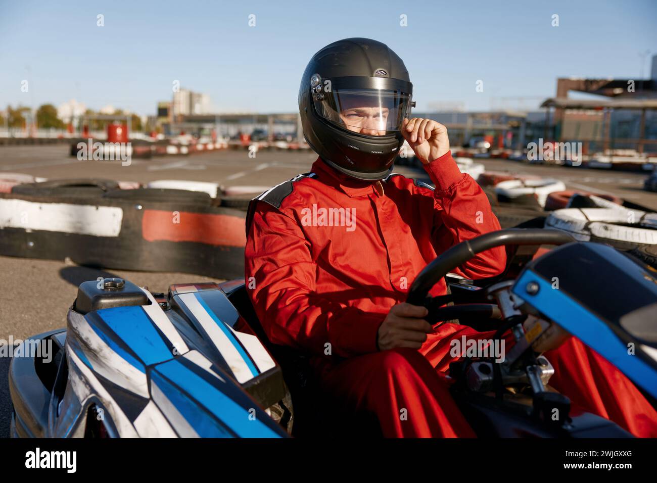 Driver taking off protective helmet while sitting at kart race car ...