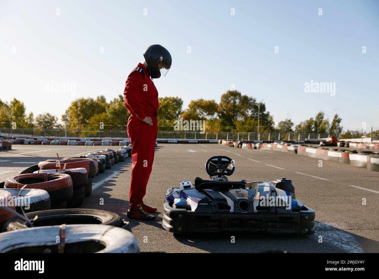 Driver wearing racing overalls and helmet standing nearby kart race car ...