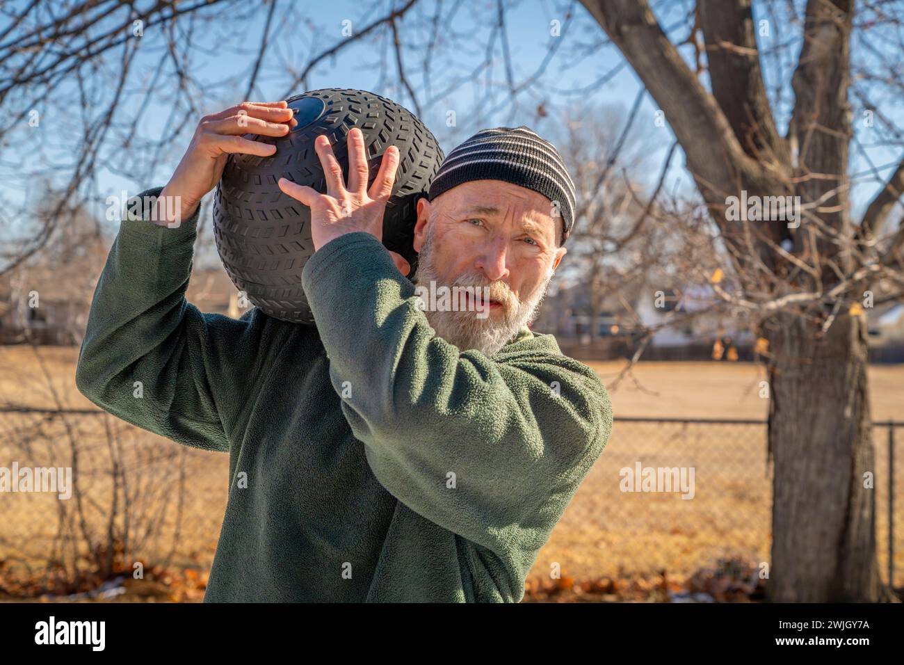 senior man is exercising with a heavy, 50 lb, slam ball in his backyard ...
