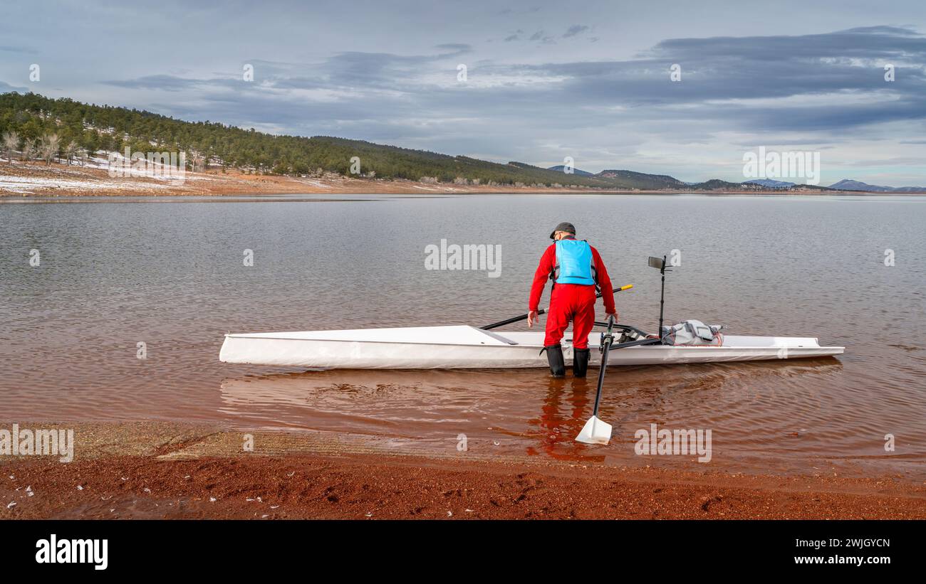 Senior male rower is launching a rowing shell on a shore of Carter Lake ...