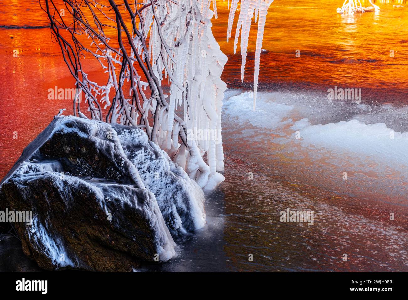 Tree branch covered with ice next to a frozen stone on a river of fire ...