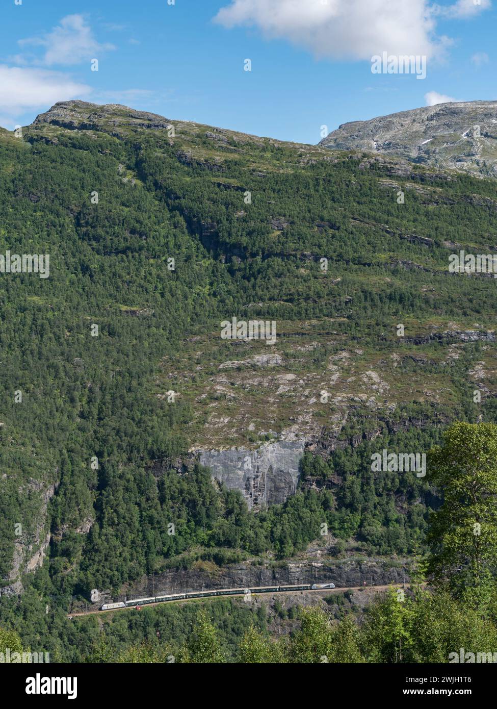 Extreme long shot shows a Flåmsbana (Flam Railway) train passing at the base of a mountain while ...
