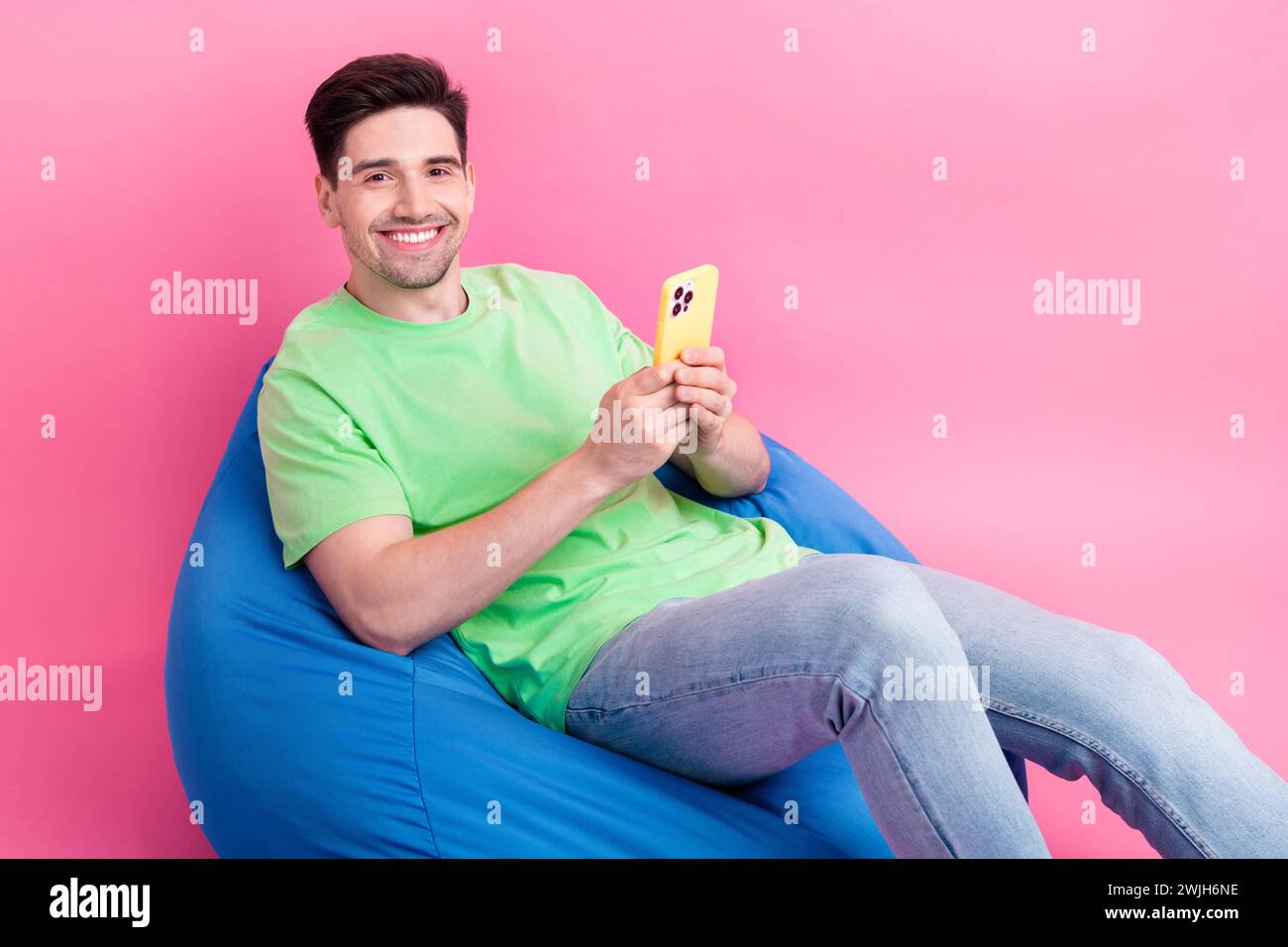 Portrait of handsome guy using smartphone chilling on bean bag texting ...