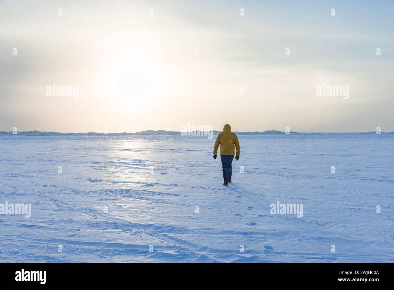 Lonely man in yellow down jacket walk the ice of frozen sea on a cold ...