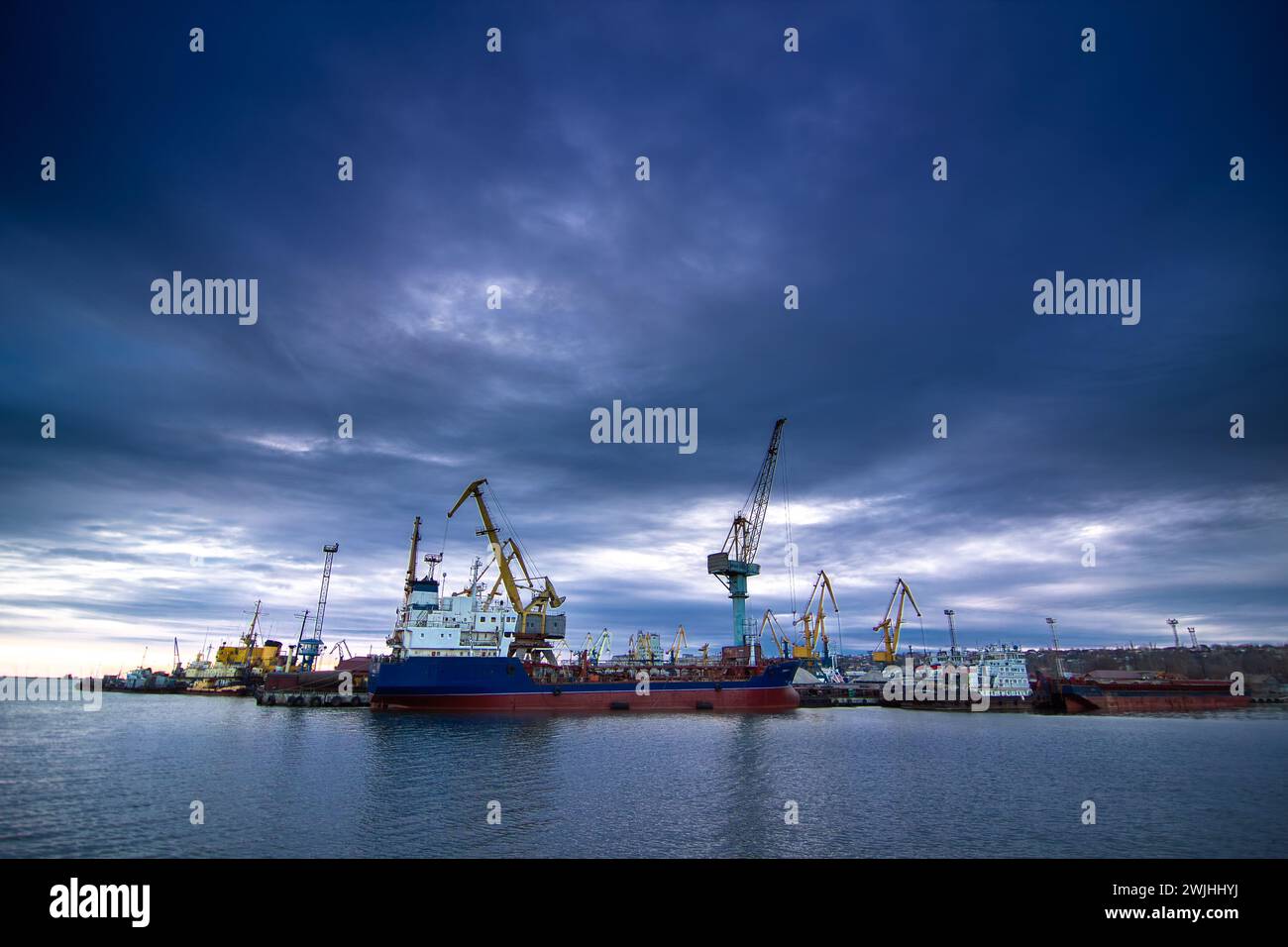 Shipping vessels and port cranes line the dock at sunset. Industrial ...