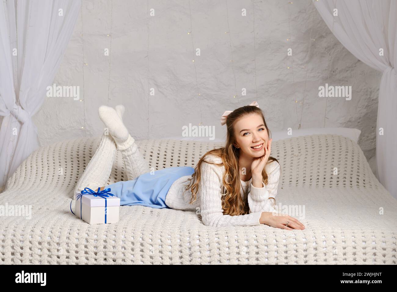A Young Woman In A Blue Dress And Warm White Socks Lying On A Bed On Her Stomach With A T Box