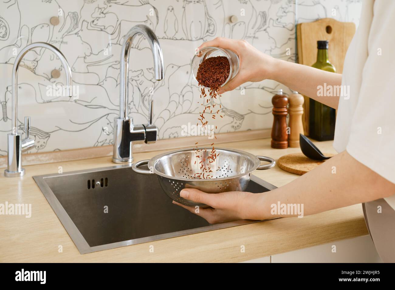 Unrecognizable woman pours rice from a glass into a colander to rinse ...