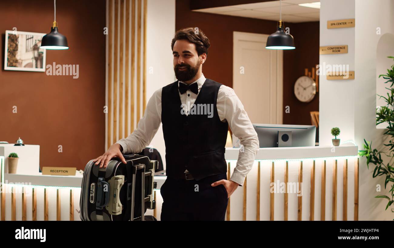 Cheerful smiling professional bellboy in formal attire with baggage ...