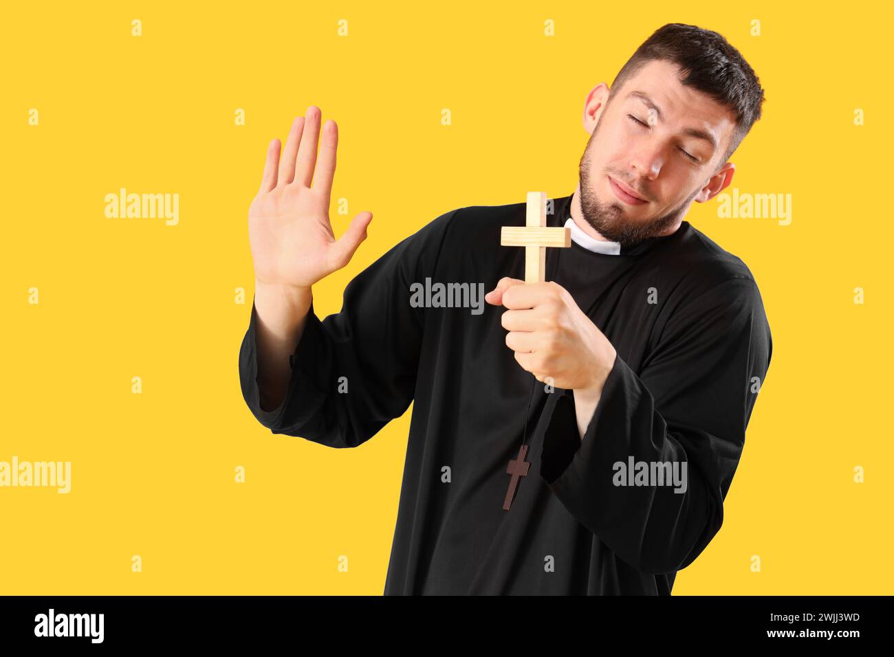 Displeased young priest with cross on yellow background Stock Photo - Alamy