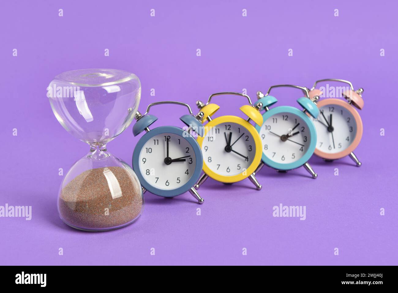Different alarm clocks and hourglass on color background. Concept of ...
