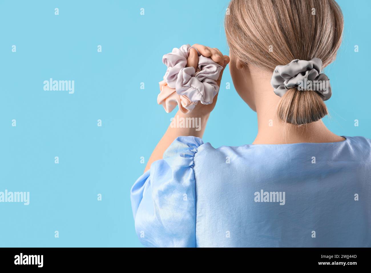 Young blonde woman with scrunchies on blue background, back view Stock ...