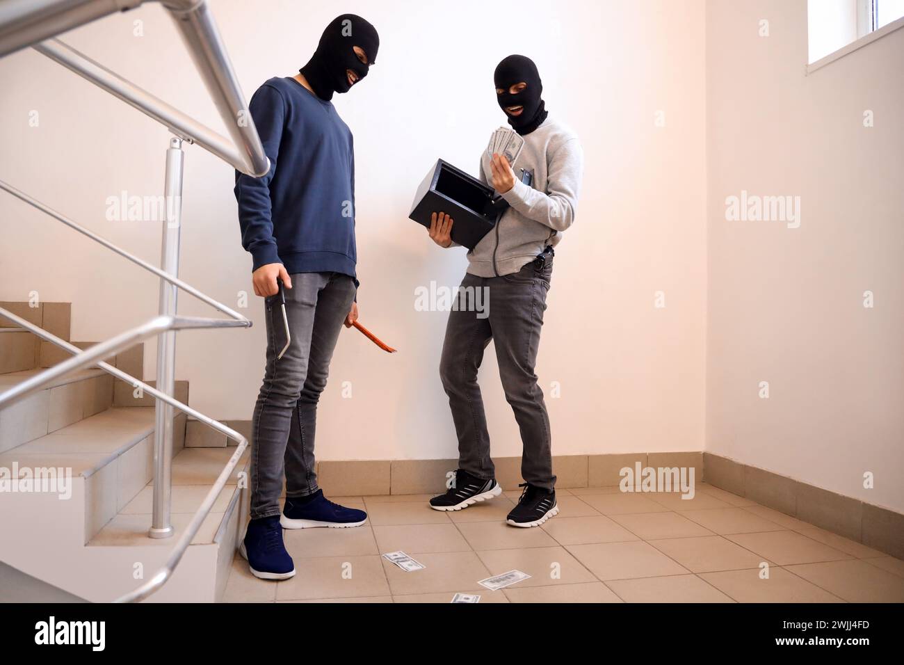 Male thieves with cracked safe and money in stairway Stock Photo - Alamy