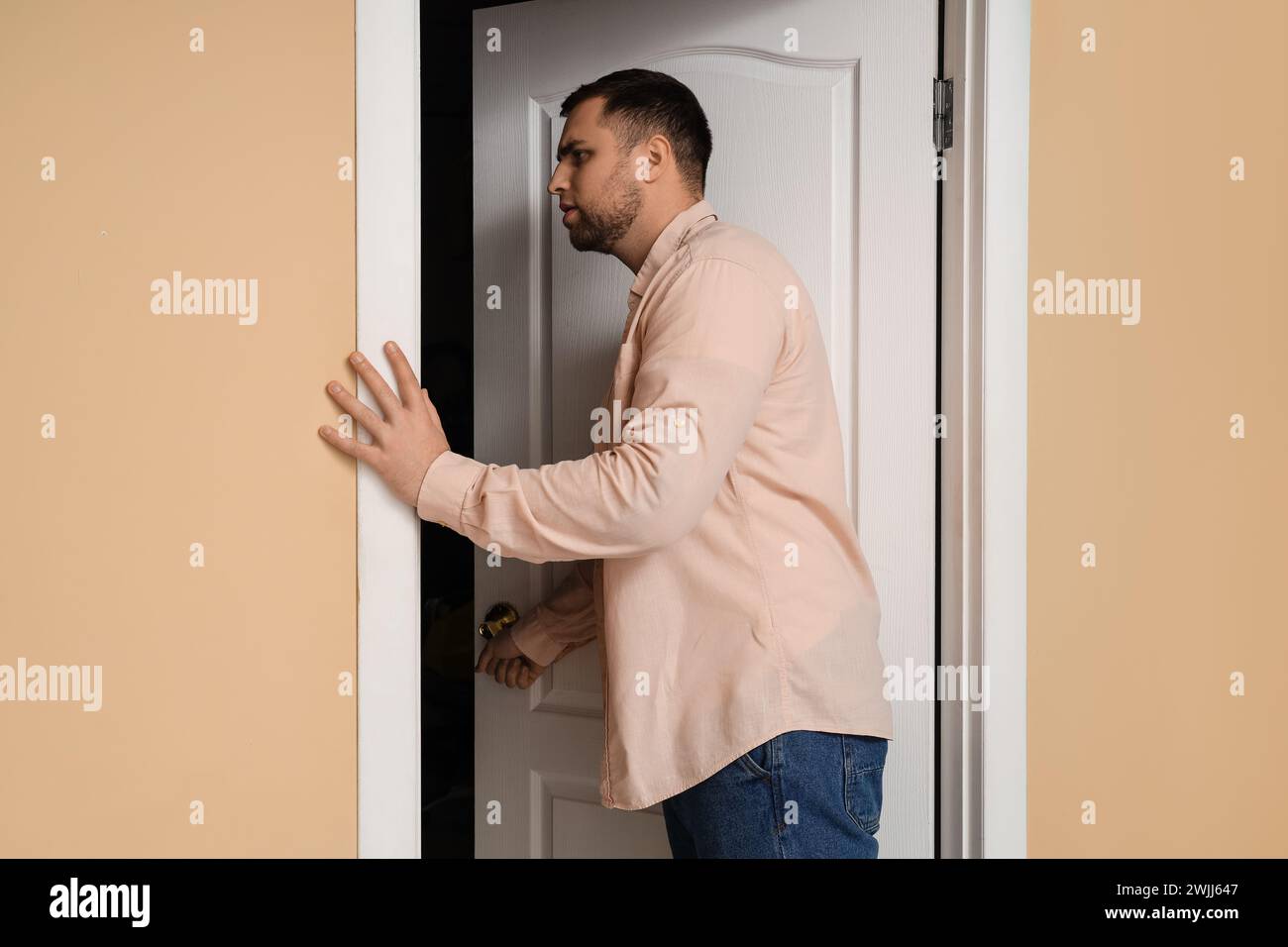 Young man looking through open door in room Stock Photo - Alamy