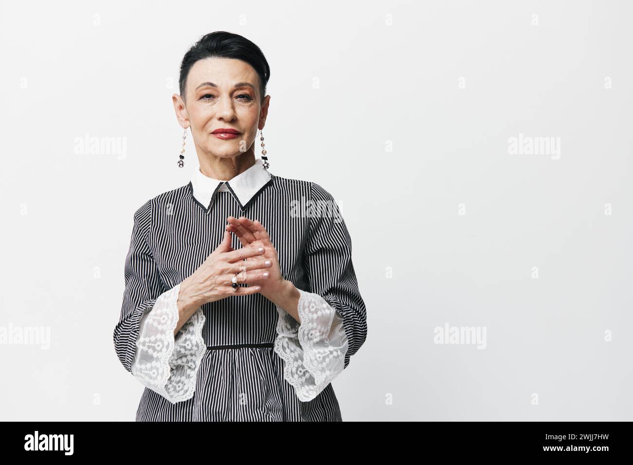 Elegant senior woman in gray dress standing with hands crossed over ...