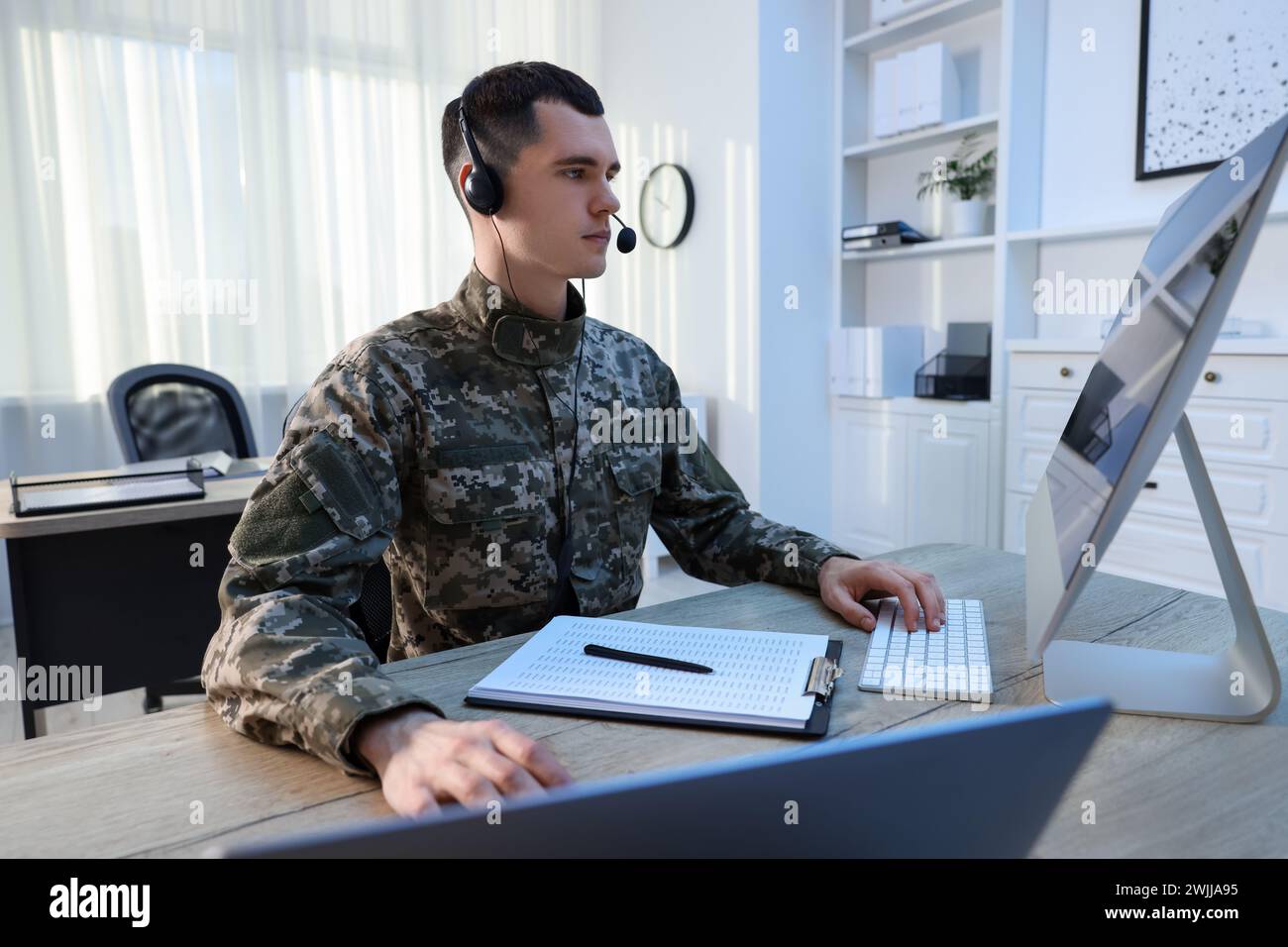 Military service. Young soldier in headphones working at wooden table ...
