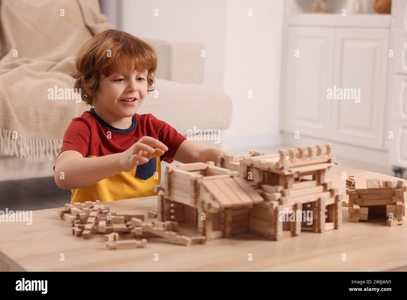 Cute little boy playing with wooden construction set at table in room ...