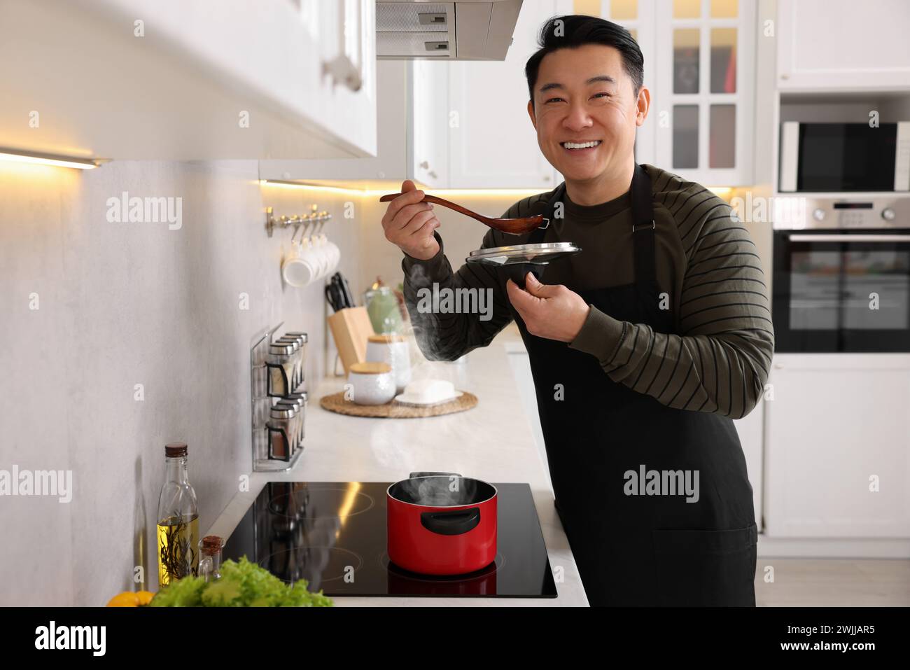 Cooking process. Happy man tasting dish in kitchen Stock Photo - Alamy