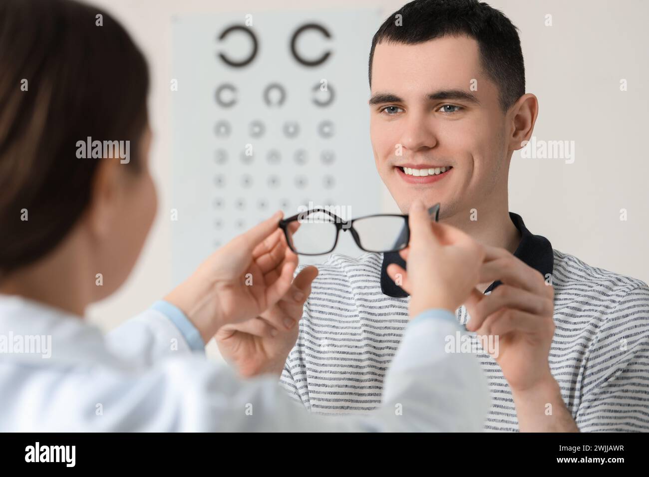 Vision testing. Ophthalmologist giving glasses to young man indoors ...