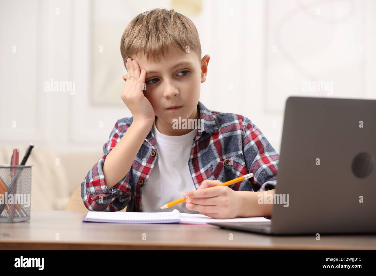 Little boy suffering from headache while studying at wooden desk ...