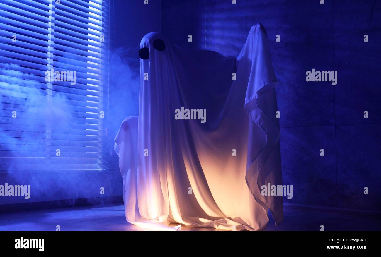 Creepy ghost. Woman covered with sheet near window in blue light Stock ...