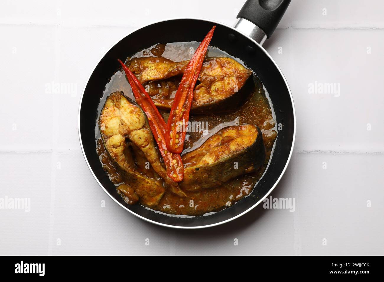 Tasty fish curry in frying pan on white tiled table, top view. Indian ...