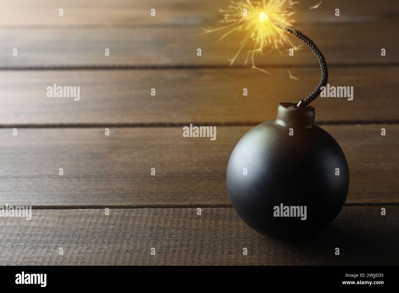 Old fashioned black bomb with lit fuse on wooden table, space for text ...