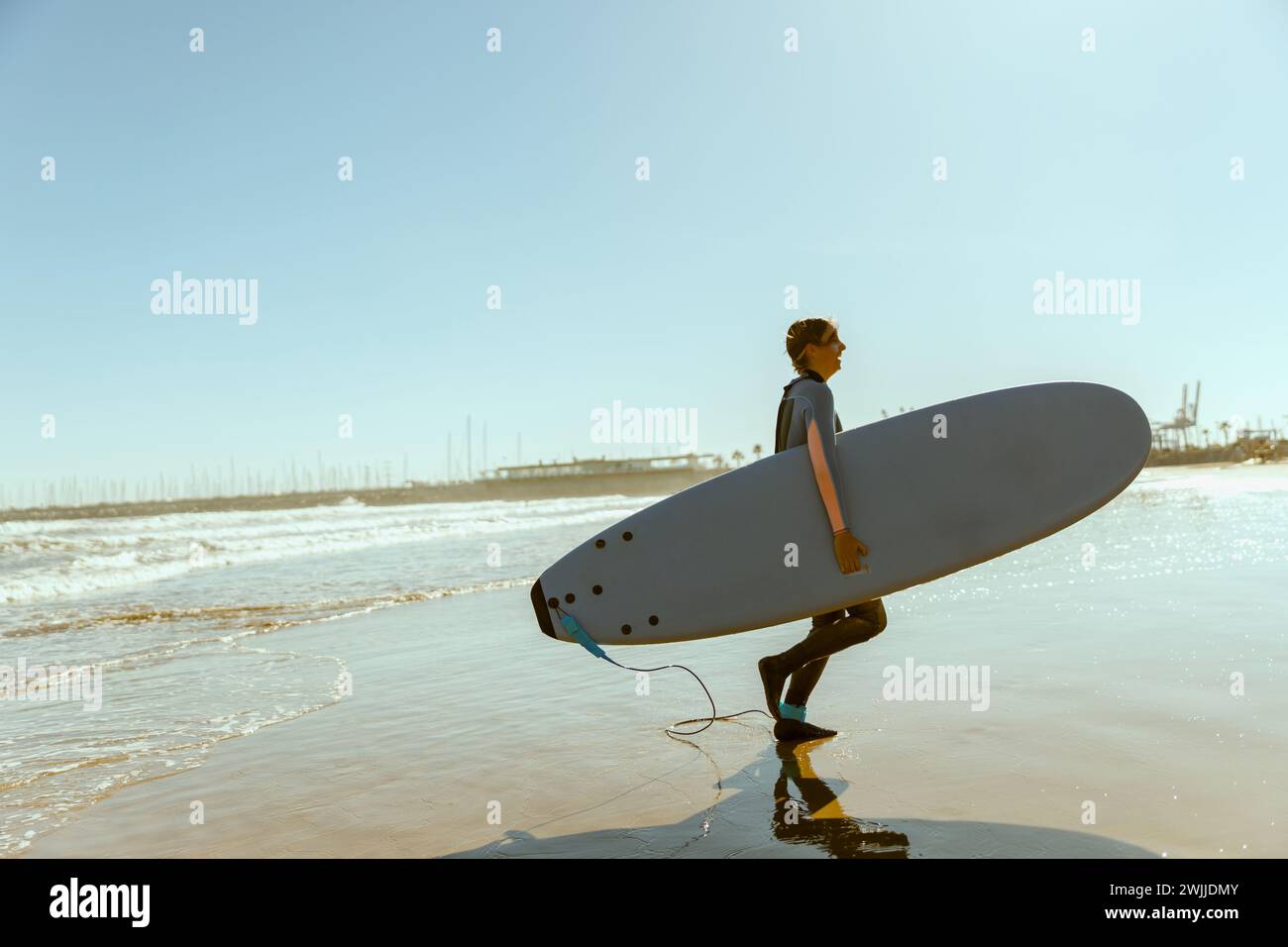 Happy female surfer in wetsuit with his surfboard entering out of sea ...