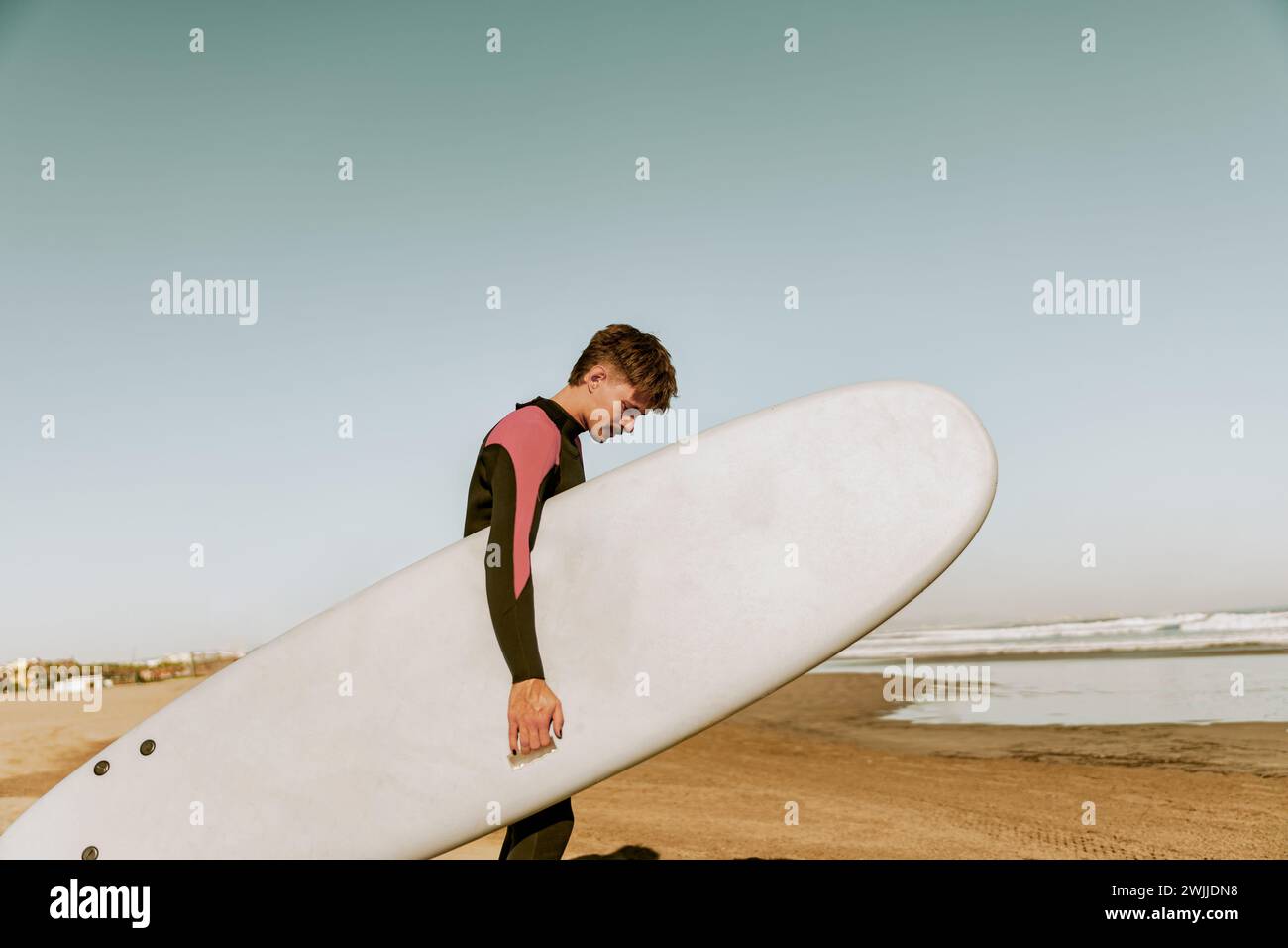 Back view of male surfer in wetsuit with his surfboard entering the sea ...
