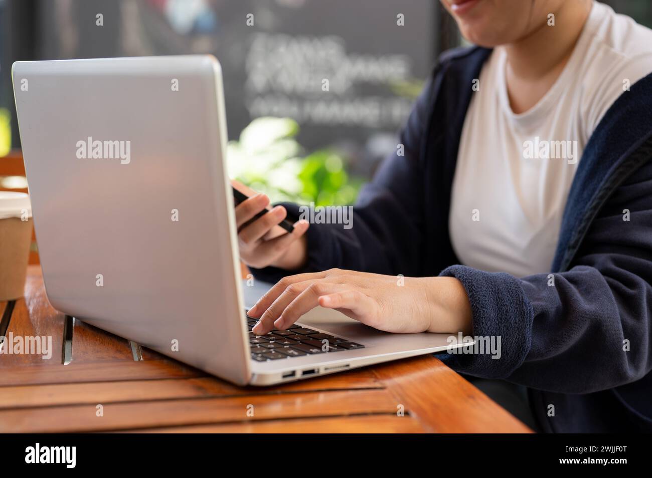 A cropped shot of an Asian woman multitasking, using her smartphone and ...