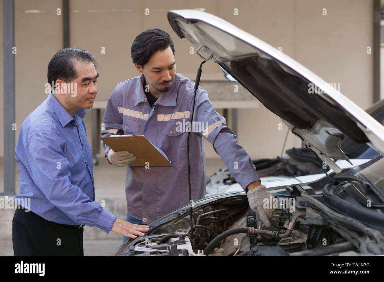 Two guys are standing by a car with the hood open, staring at the ...