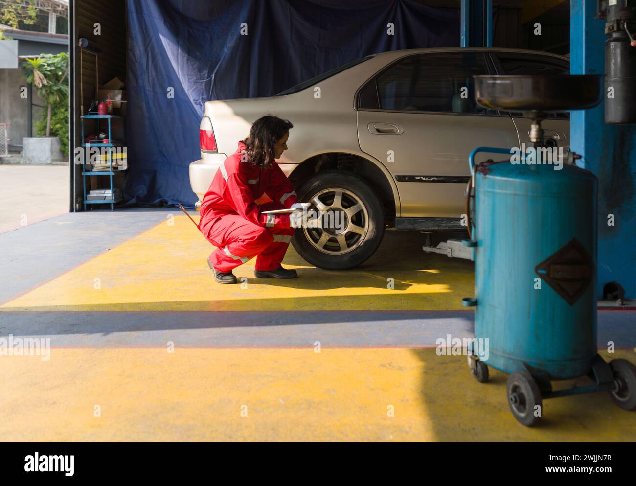 Young mechanic in a red coverall working on a car inside a workshop or ...