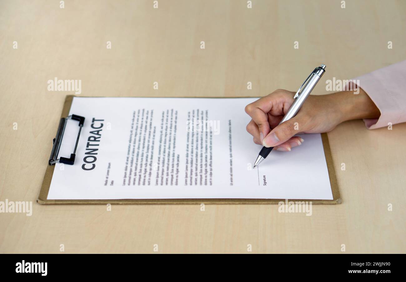 Closeup woman hand signing her name on a contract document on a board ...