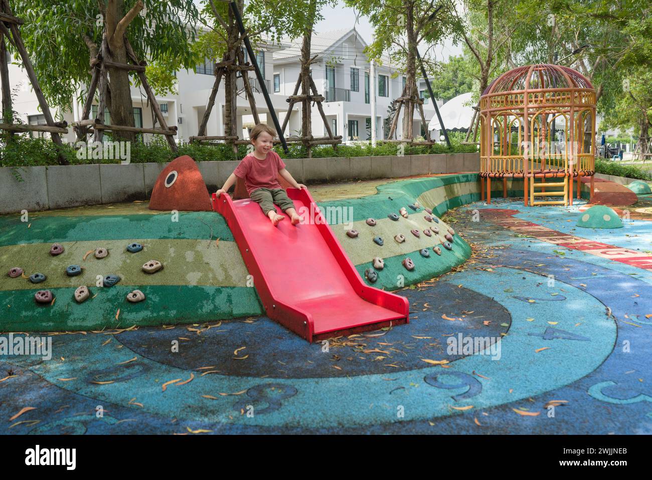 A child is going down a slide with a happy face at a playground full of ...