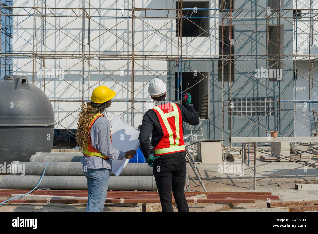 Two construction workers are standing together in front of a large ...