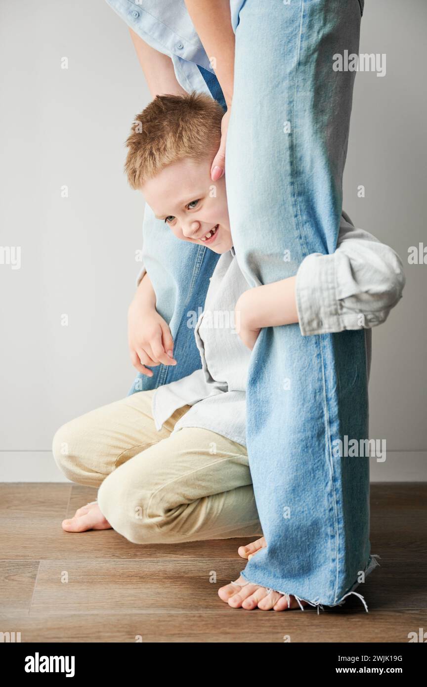 Young happy boy hugging mom's legs. Hyperactive kid holding his mother ...