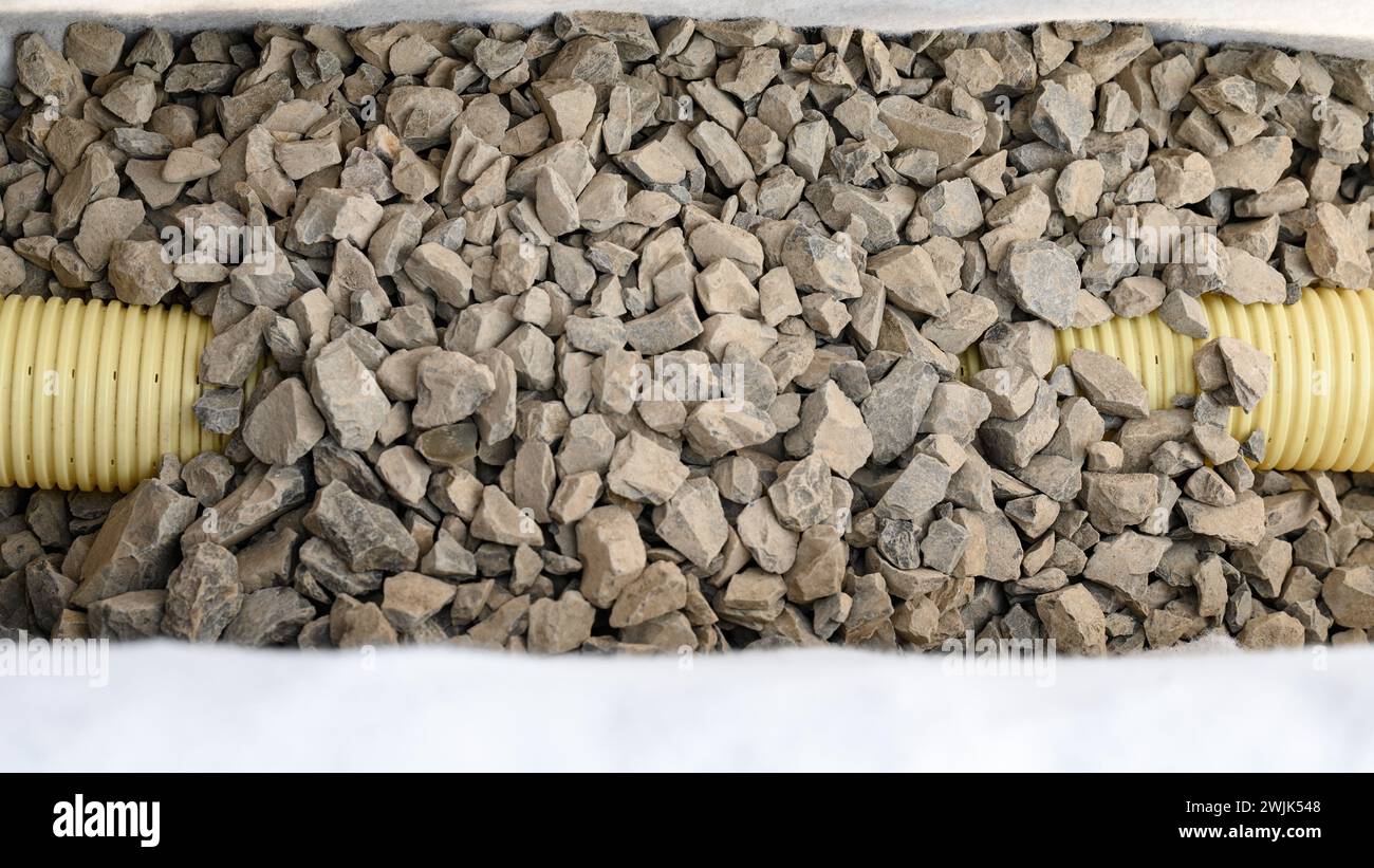 Yellow corrugated pipe with perforation in a trench with crushed stone ...