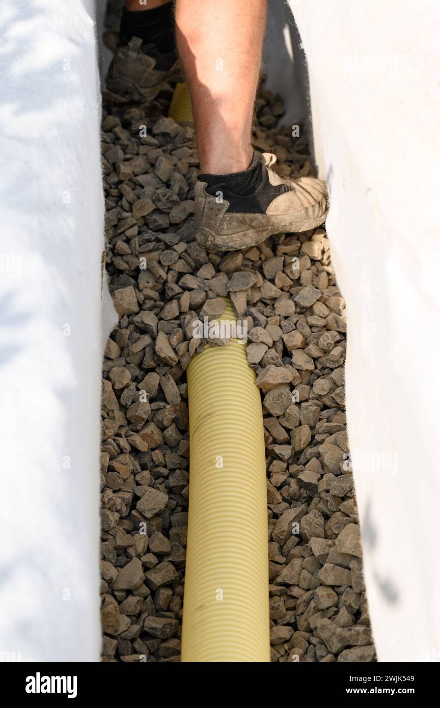 A worker stands in a drainage trench with white geotextile. Feet of the ...