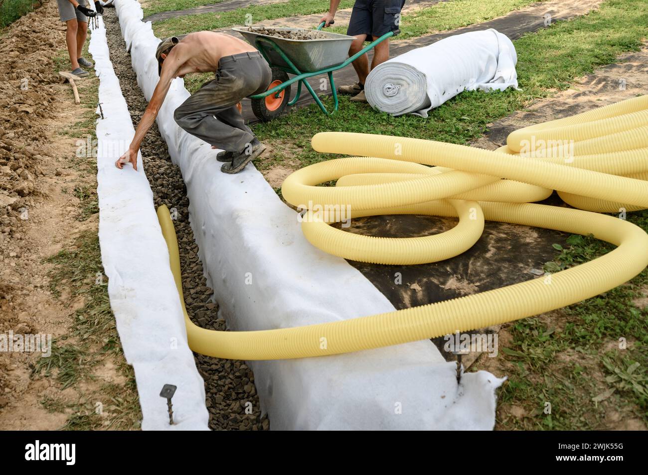 A man pours rubble crushed stone from a wheelbarrow into a trench ...
