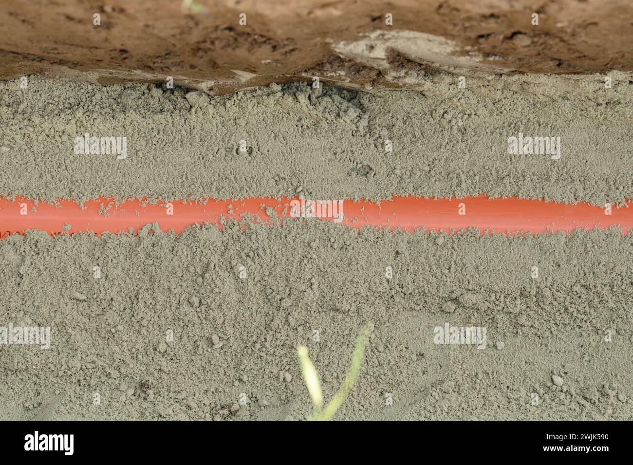 An orange reinforced sewer pipe is compacted with sand in a trench ...