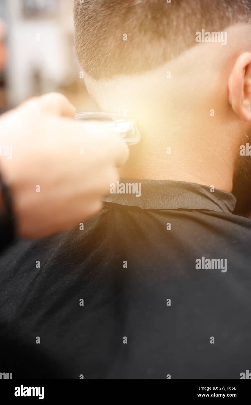 Barber shaves the temple with a cordless trimmer during a short haircut ...