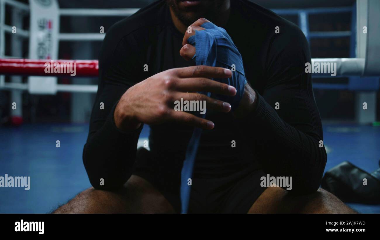 African American boxer sits near boxing ring and wraps his hands with ...