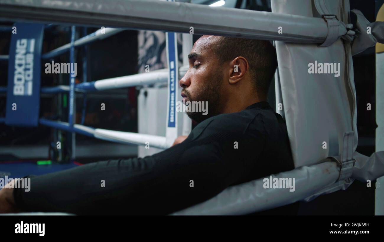 Tired and exhausted African American boxer sits in boxing ring corner ...