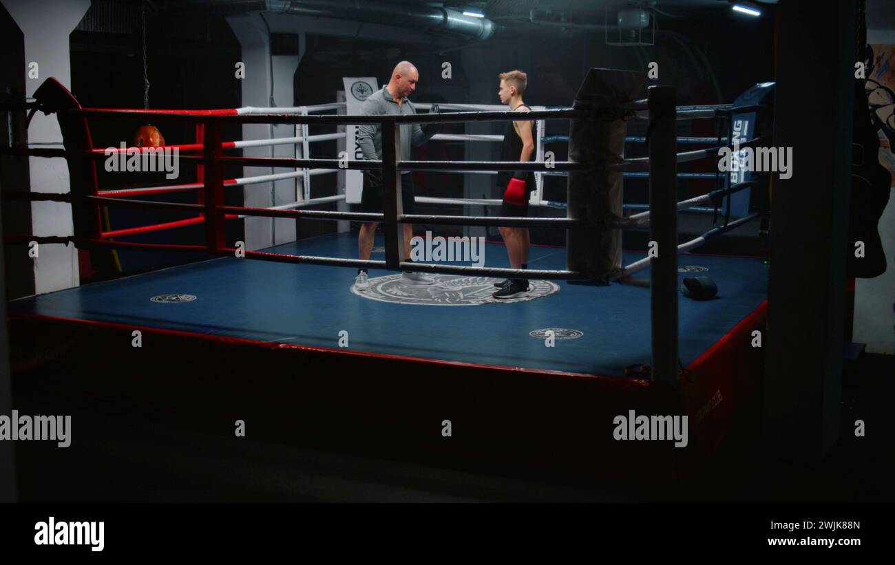 Boy in boxing gloves stands on ring and talks with trainer. Adult man ...
