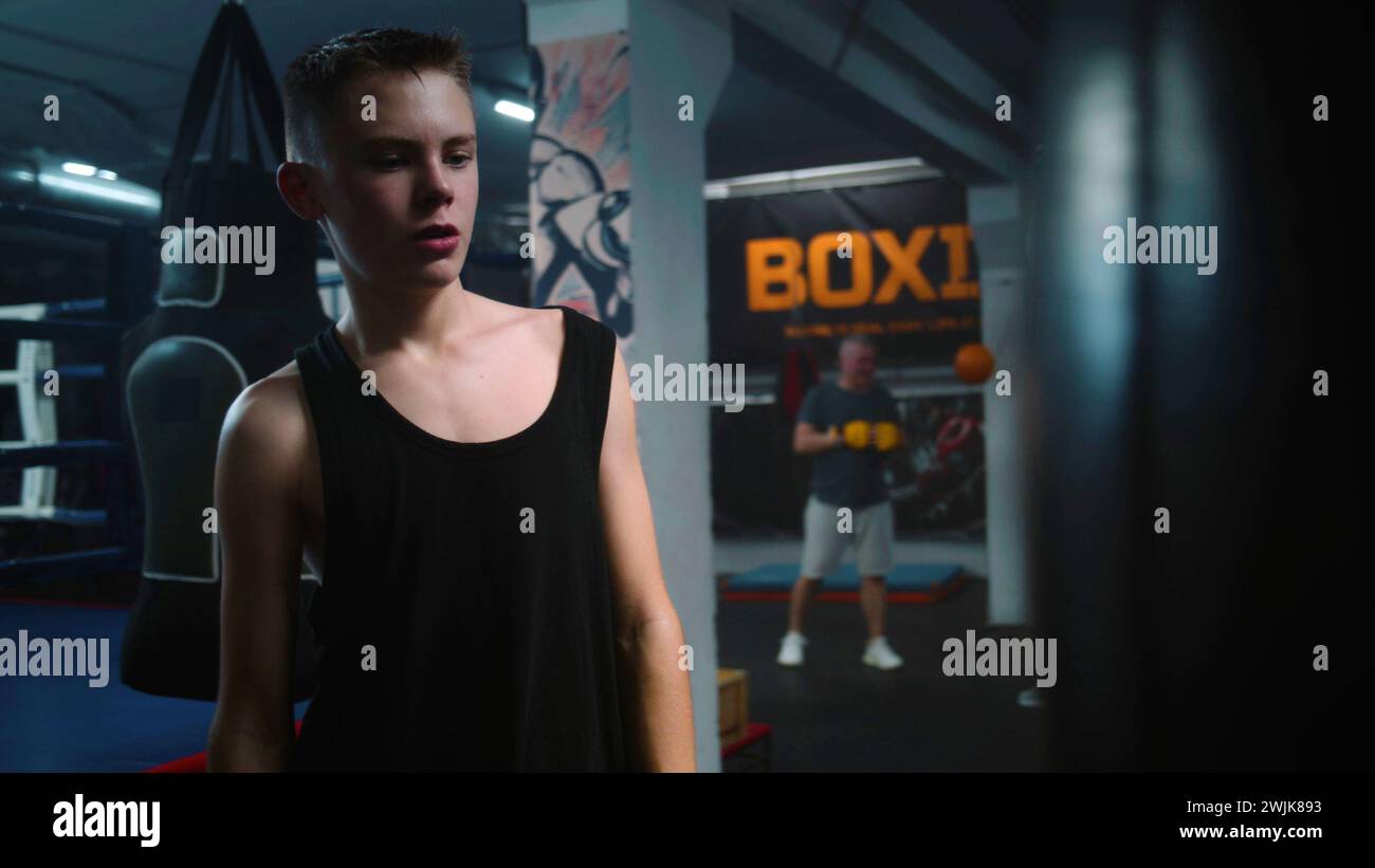 Confident young fighter hits punching bag while training in dark boxing ...